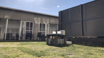 Área externa cercada com um edifício, cadeiras e um contentor de lixo.