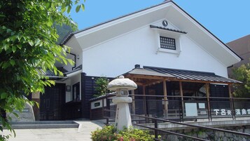 Um edifício japonês tradicional com fachada branca, telhado preto e um candeeiro de pedra em primeiro plano.