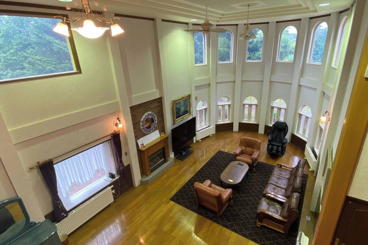 Uma sala de estar ampla, com lareira, sofás de couro, televisão e janelas grandes.