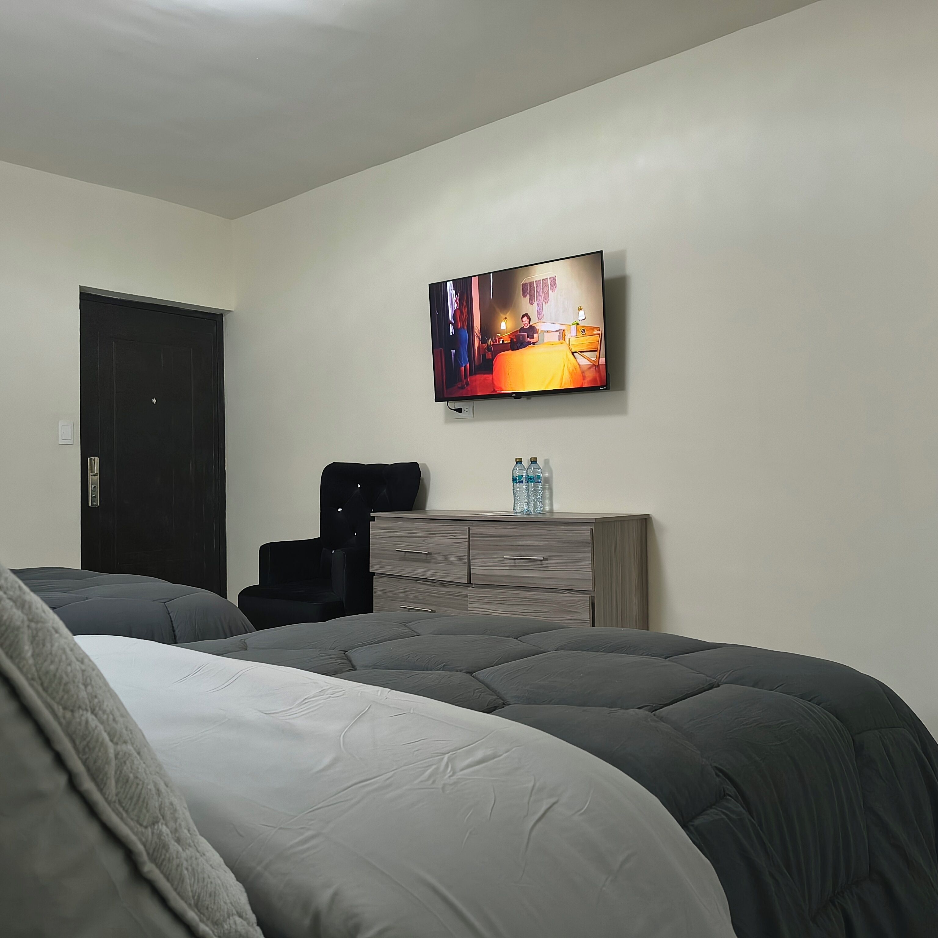 Quarto com uma cama, penteadeira, televisão fixada na parede e uma porta.
