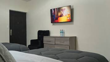Quarto com uma cama, penteadeira, televisão fixada na parede e uma porta.