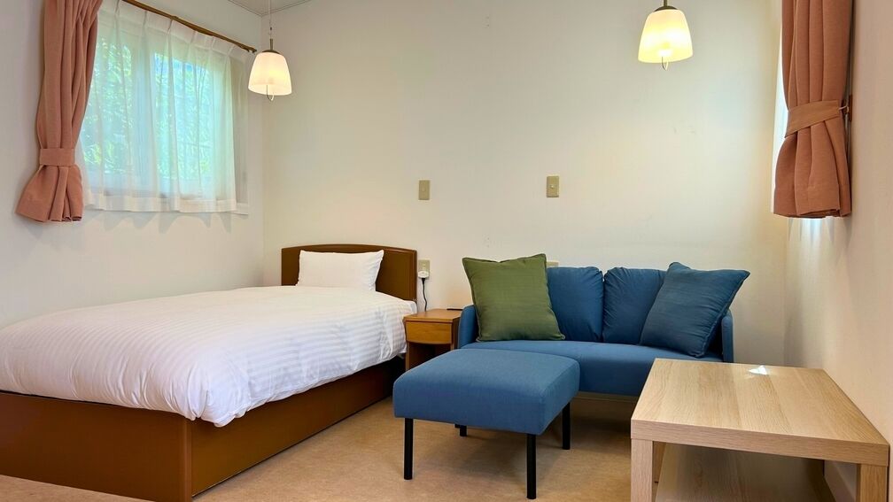 Quarto com cama, sofá, mesa pequena e duas luminárias pendentes.