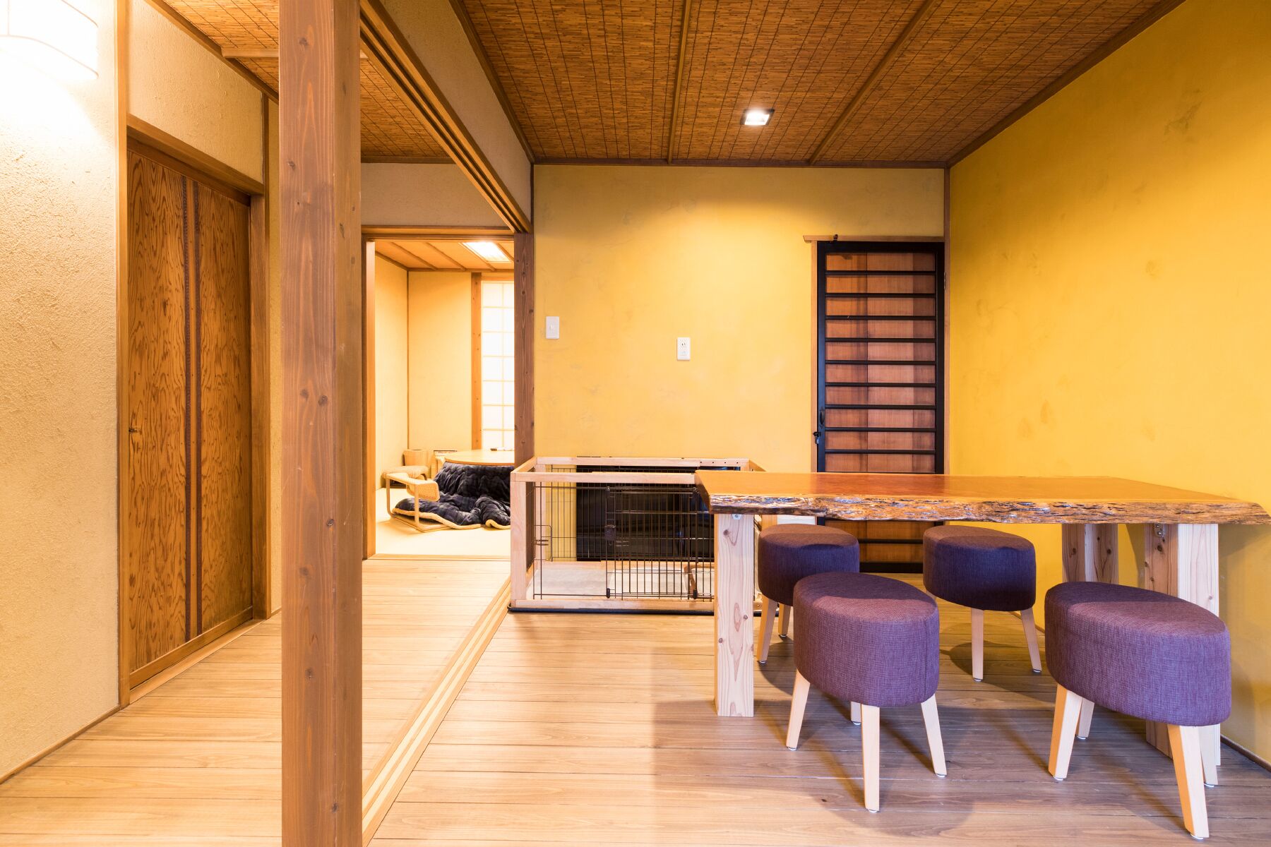 Quarto com piso de madeira, uma mesa com quatro cadeiras, uma cama e uma porta de correr.