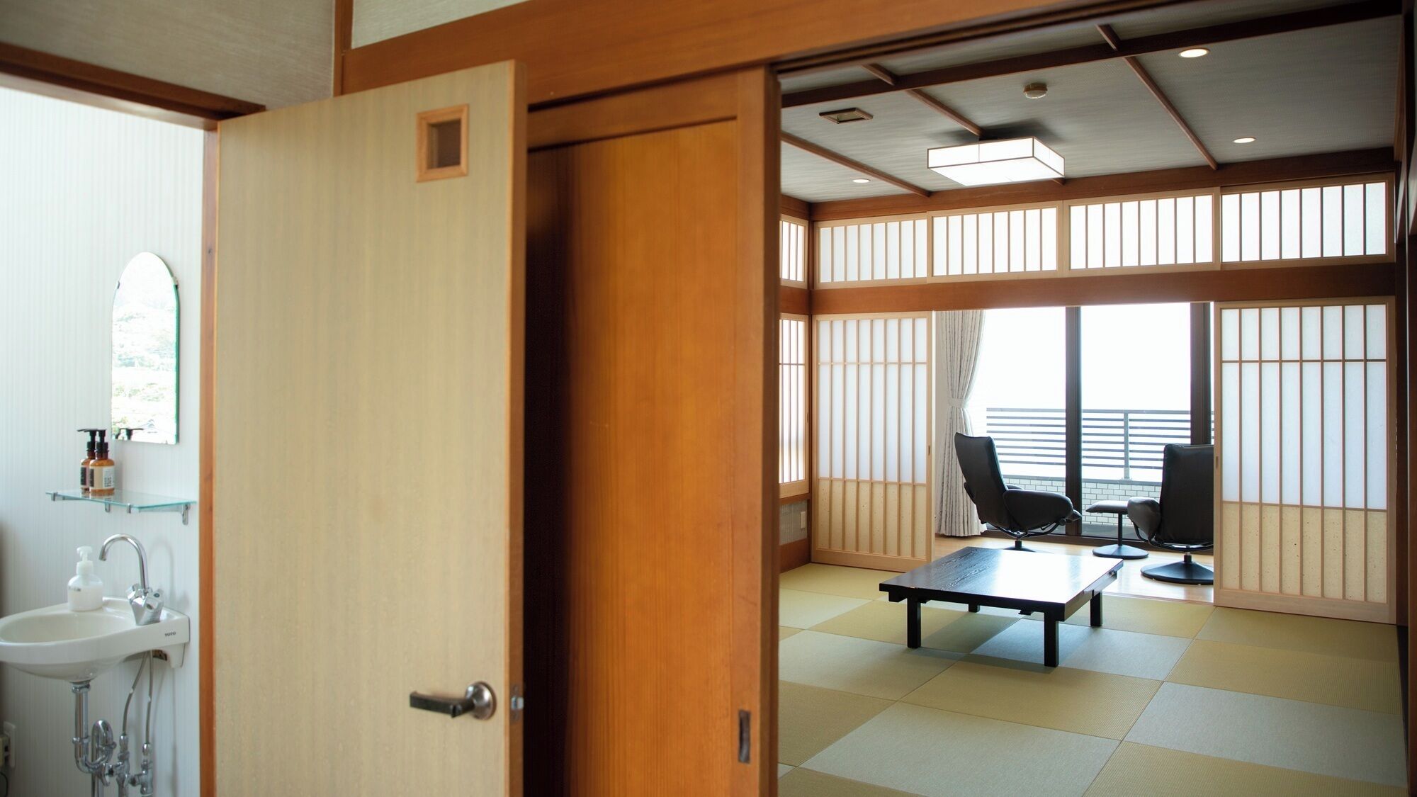 Um quarto japonês tradicional com piso de tatame, uma mesa de tatame, uma cadeira preta e um painel deslizante shoji.