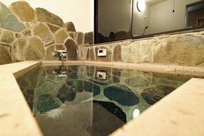 Um muro de pedra, uma piscina com fundo de vidro e um termostato na parede.