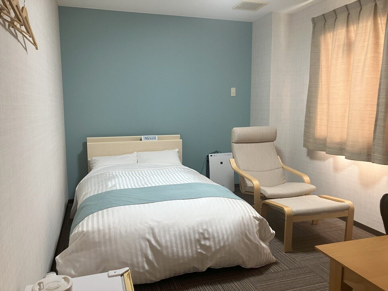 Quarto de hotel com cama, uma cadeira, uma mesa e janela com cortinas.