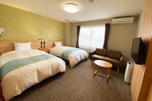 Quarto de hotel com duas camas, um sofá, uma mesa pequena, uma televisão e um ar condicionado.