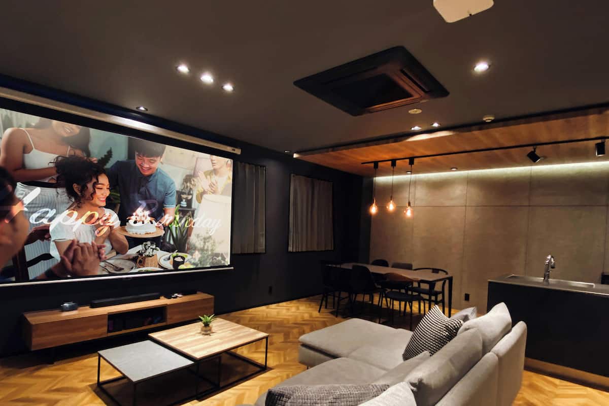 Quarto de hotel moderno com uma televisão grande, um sofá, uma mesa de centro, um espaço para refeições e uma cozinha.