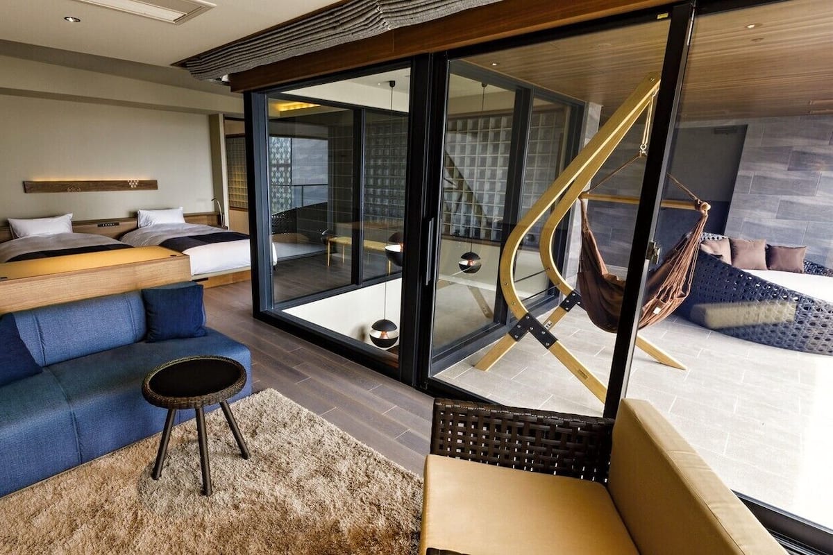 Quarto de hotel moderno com sofá, mesa redonda pequena, parede de vidro e rede.