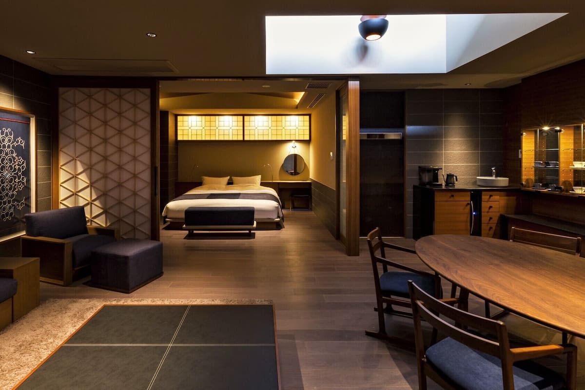 Quarto de hotel com cama, escrivaninha, mesa de jantar e cozinha compacta.