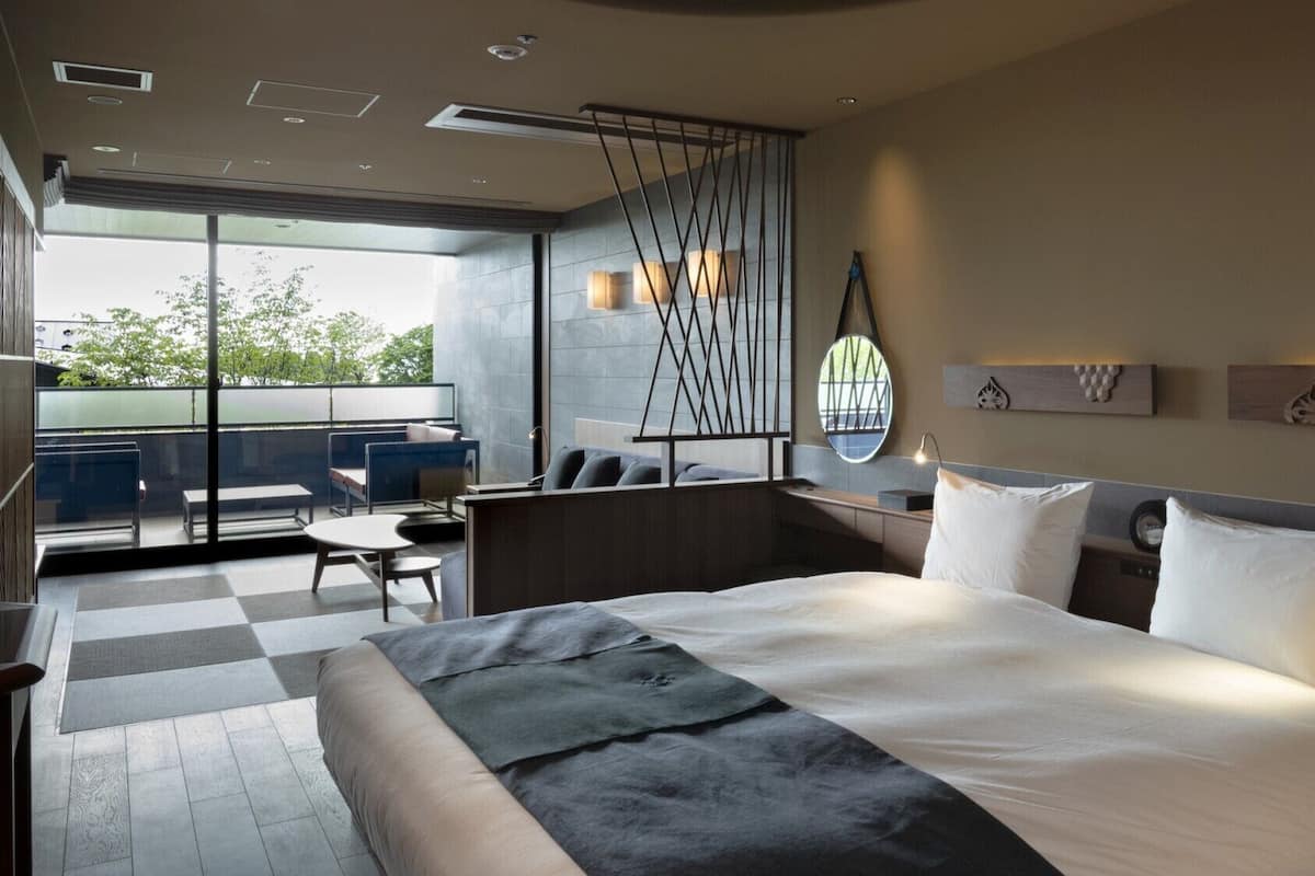 Quarto de hotel moderno com uma cama grande, varanda com assentos e vista para o exterior.