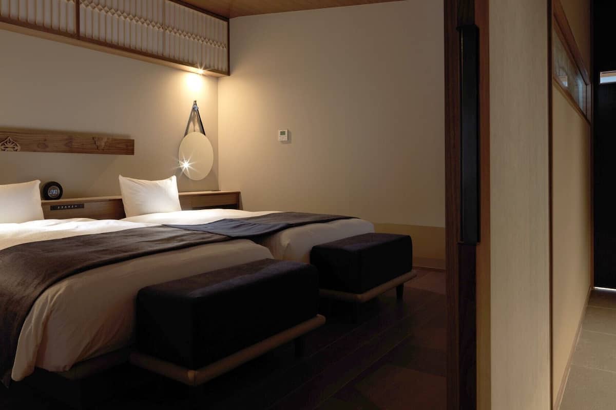 Quarto de hotel com uma cama grande, mesas de cabeceira, luminária na parede e termostato.