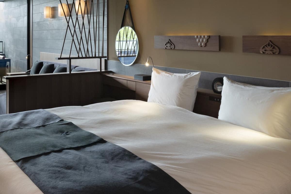 Cama bem arrumada com roupa de cama branca e cinza escura, mesa de cabeceira com abajur e arte decorativa na parede.