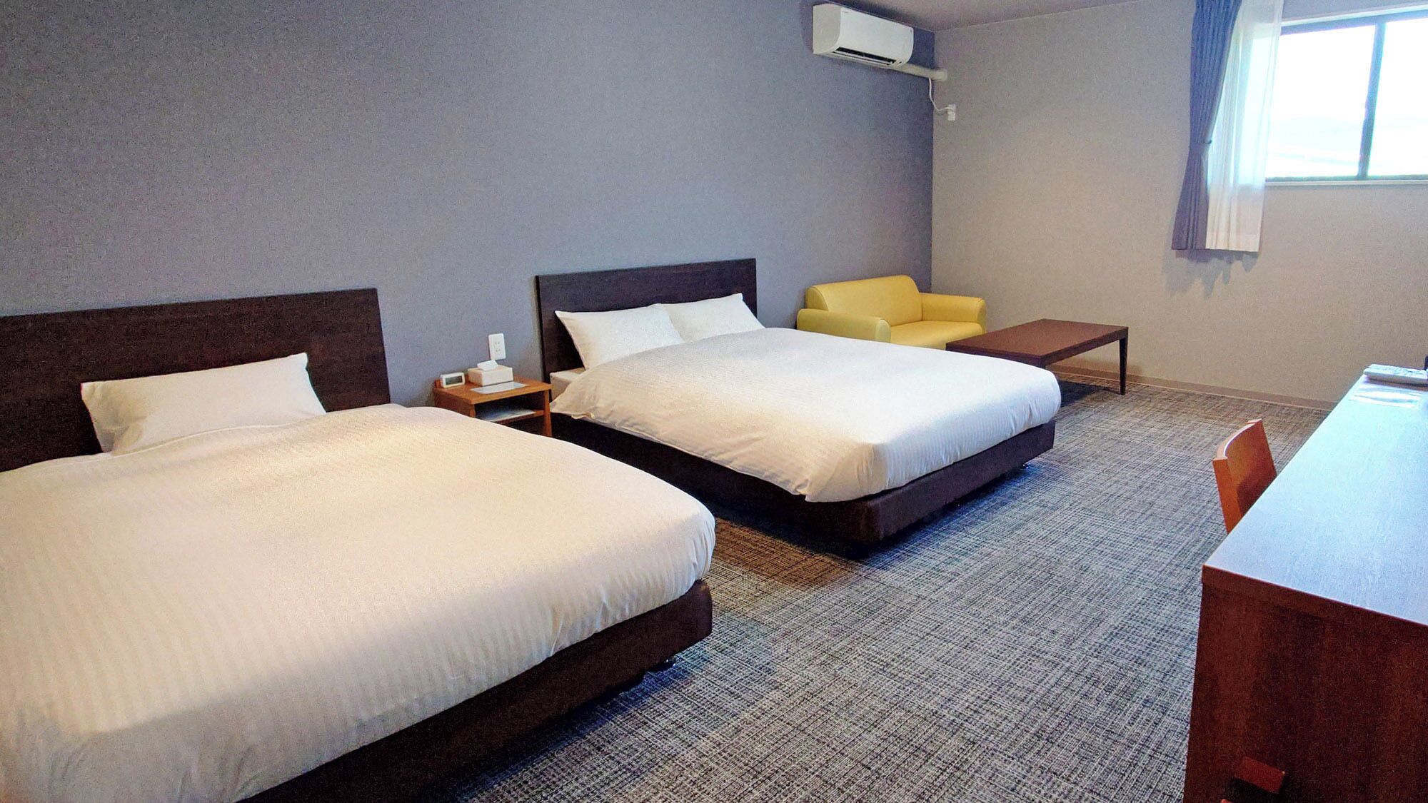 Quarto de hotel com duas camas, uma escrivaninha, uma cadeira e um aparelho de ar condicionado.