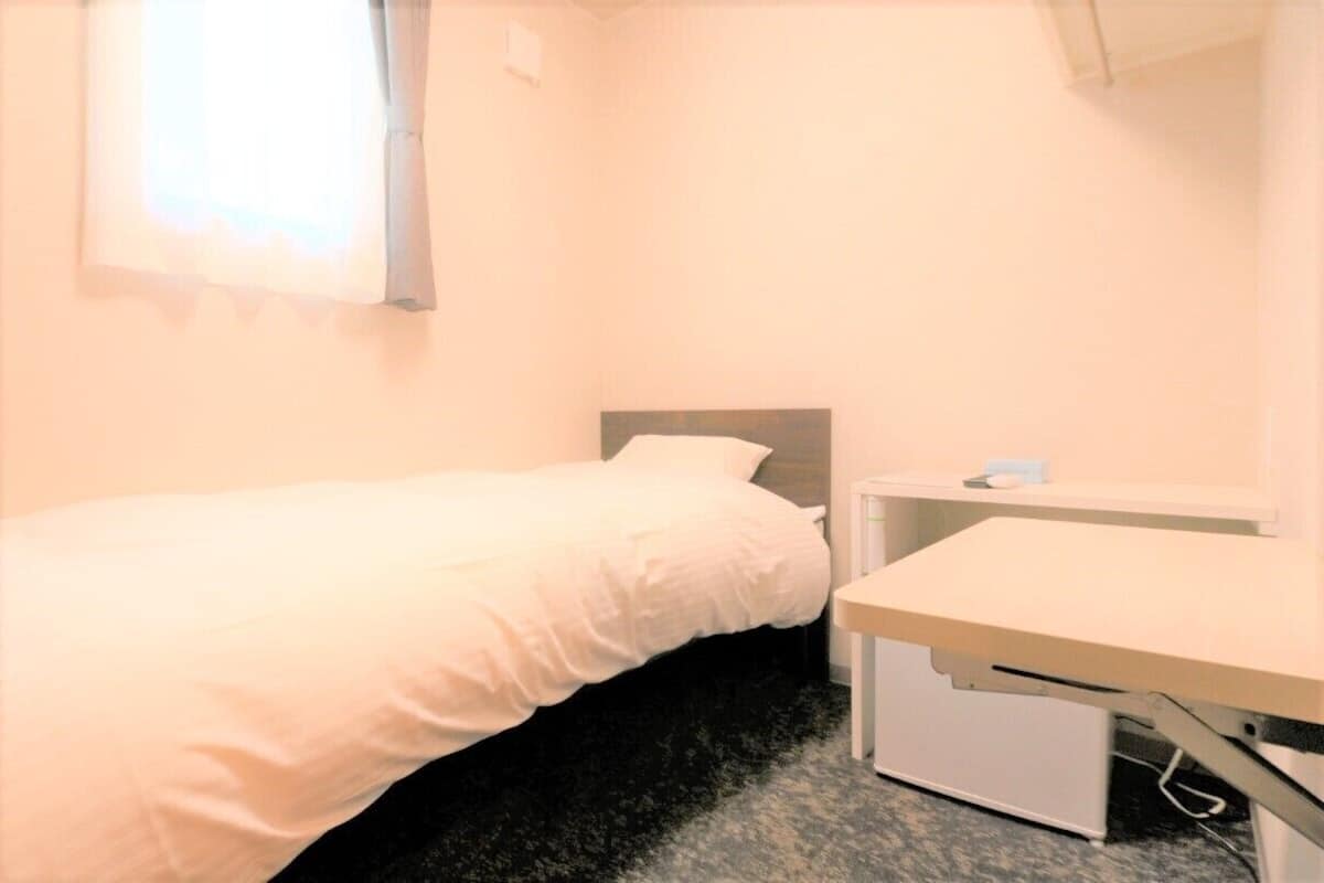 Quarto pequeno com uma cama de solteiro, uma mesa e uma cadeira.