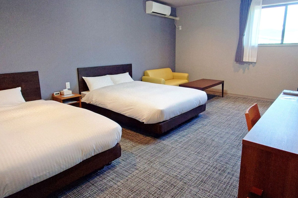 Quarto de hotel com duas camas, uma escrivaninha, uma cadeira e um ar condicionado.