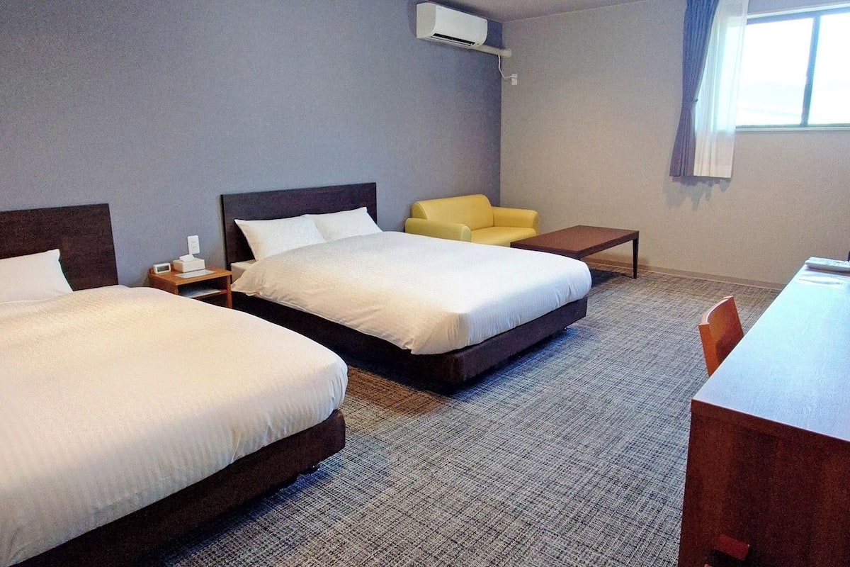 Quarto de hotel com duas camas, uma escrivaninha, uma cadeira e ar condicionado.