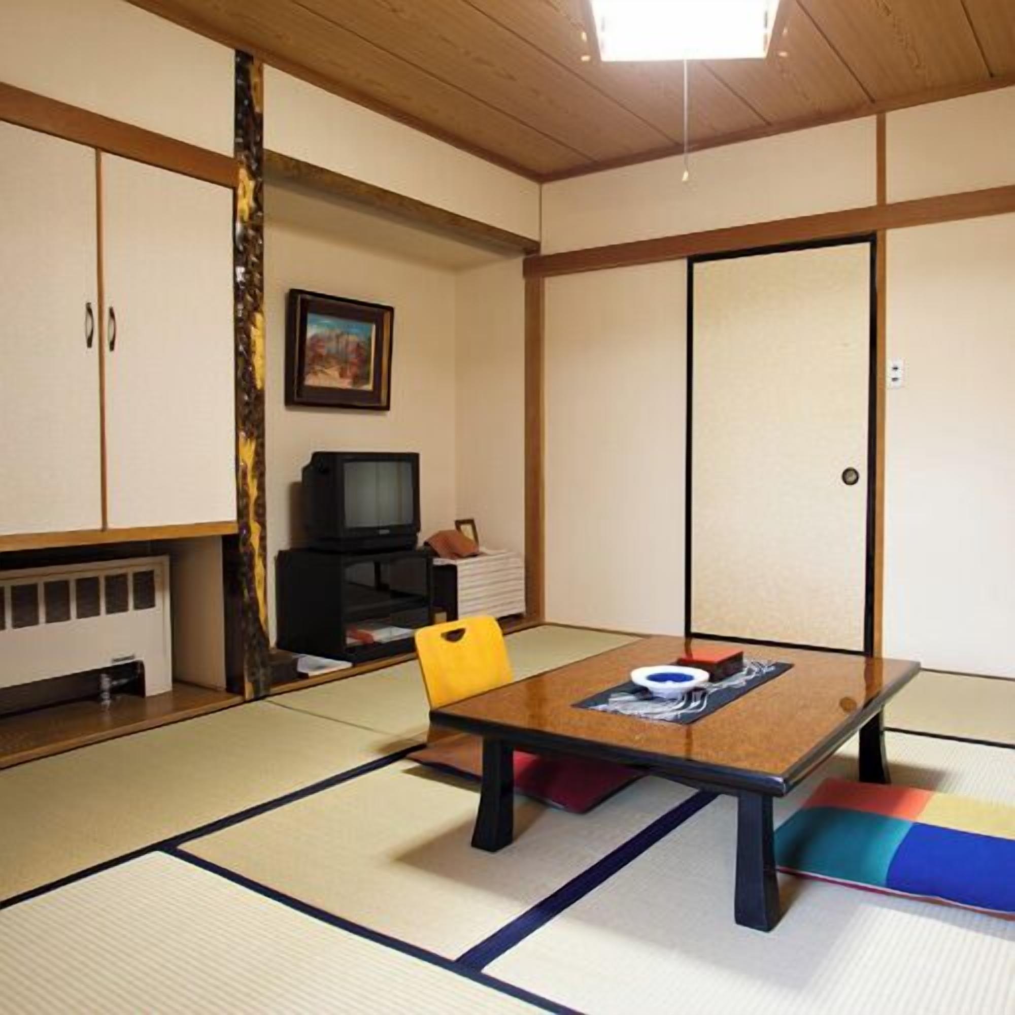 Um quarto japonês tradicional, com tatames, uma mesa baixa, uma televisão e portas deslizantes.
