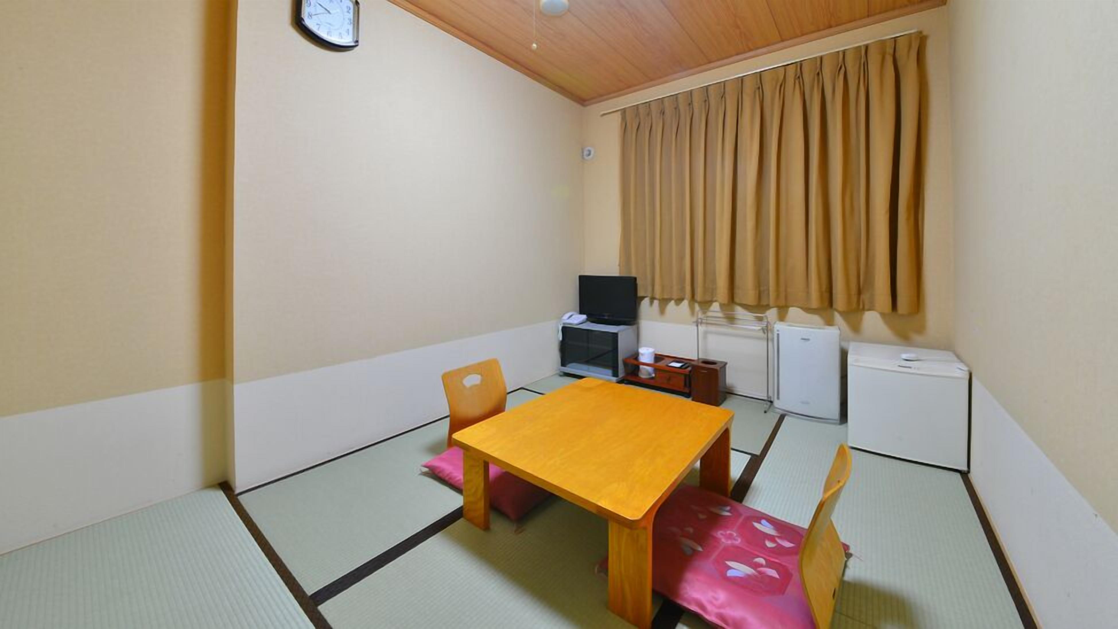 Um quarto pequeno com uma mesa de madeira, televisão, frigorífico e um relógio na parede.