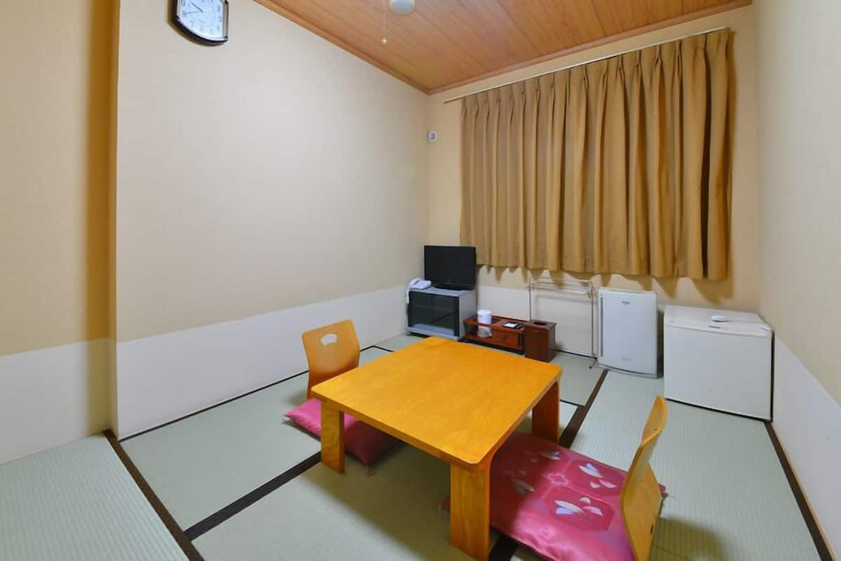 Um quarto pequeno com uma mesa de madeira, televisão, frigorífico e um relógio na parede.