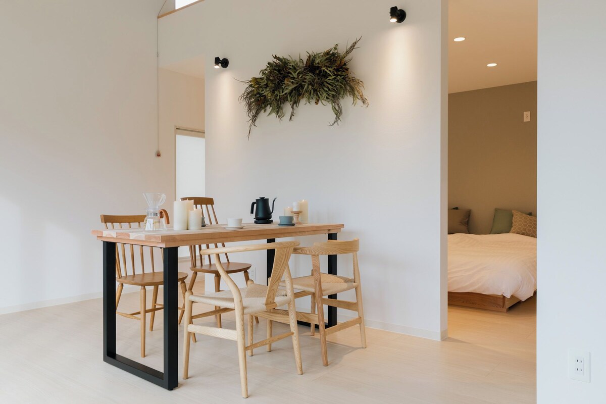 Quarto moderno e minimalista com mesa de jantar de madeira, cadeiras e uma cama.