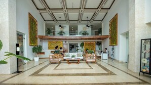 Um hall amplo com área de estar central, balcão de recepção e plantas em vasos.