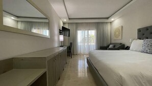 Quarto de hotel moderno com uma cama grande, uma escrivaninha com cadeira, televisão e um espelho amplo.