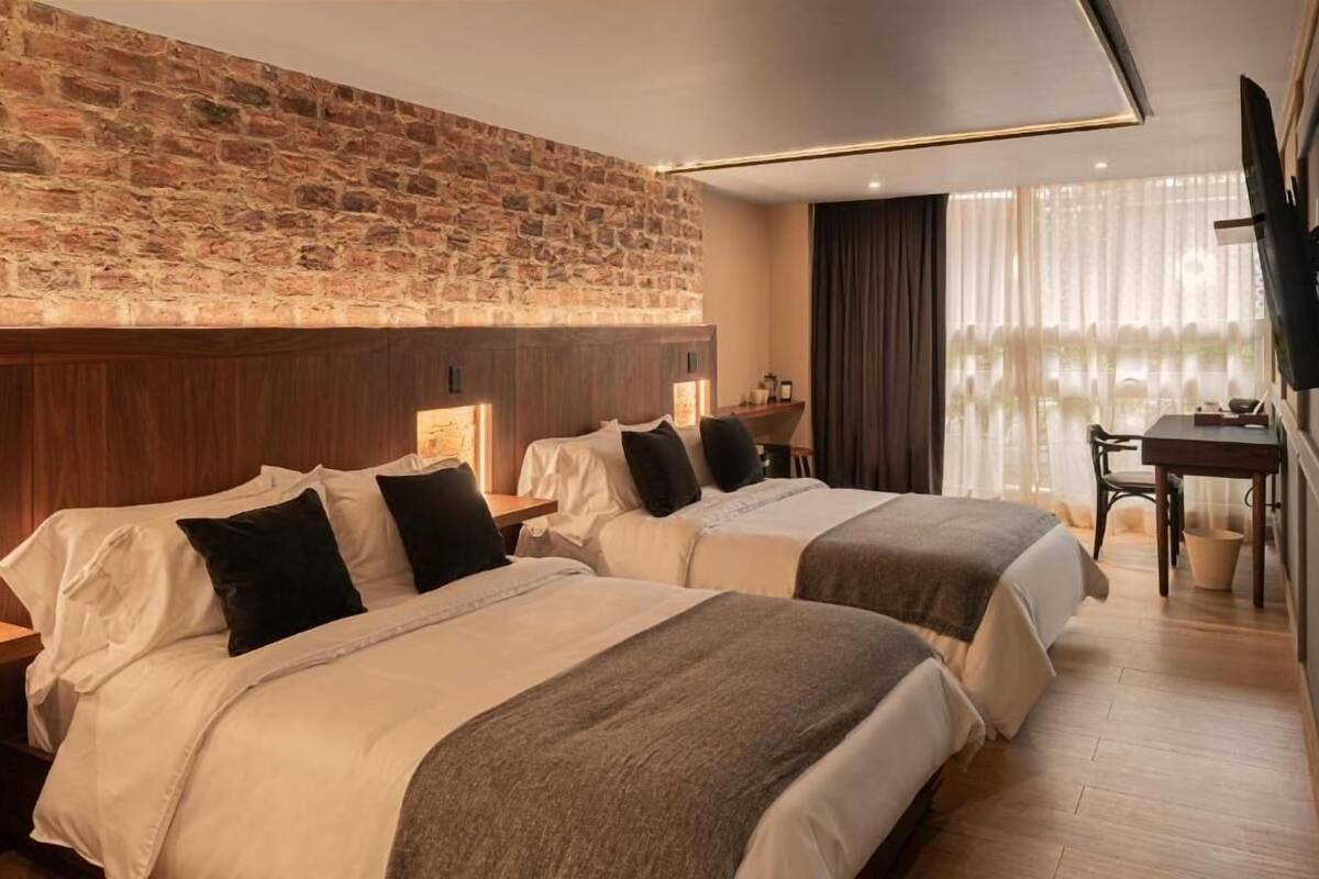 Quarto de hotel com duas camas, parede de pedra, televisão de tela plana, mesa de jantar e janela com cortinas.