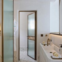 Casa de banho com porta de vidro, lavatório com artigos de higiene e toalha pendurada na parede.