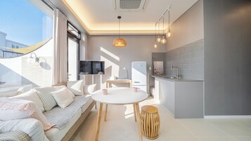 Um apartamento moderno com sofá, mesa de jantar, cozinha e televisão.