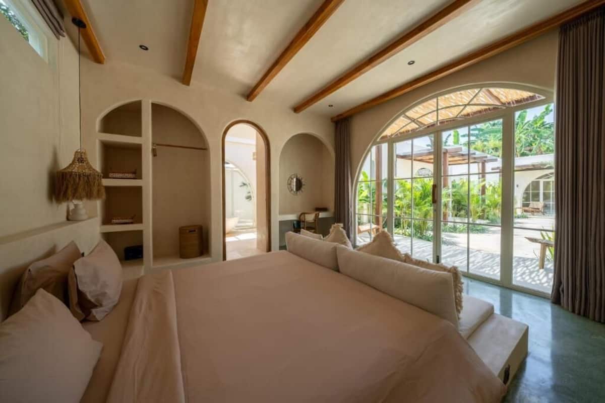 Quarto com cama grande, estantes embutidas, luminária pendente e vista através de amplas janelas.