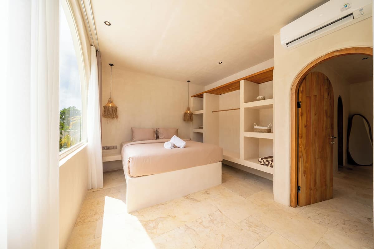 Um quarto com cama, luminária pendente, porta de madeira e prateleiras embutidas.