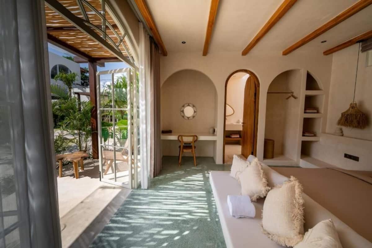 Quarto com sofá, escrivaninha e vista para o exterior.