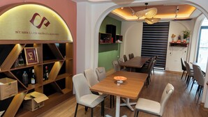 Uma sala de jantar com mesa e cadeiras de madeira, uma estante com diversos objetos e uma luminária decorativa no teto.