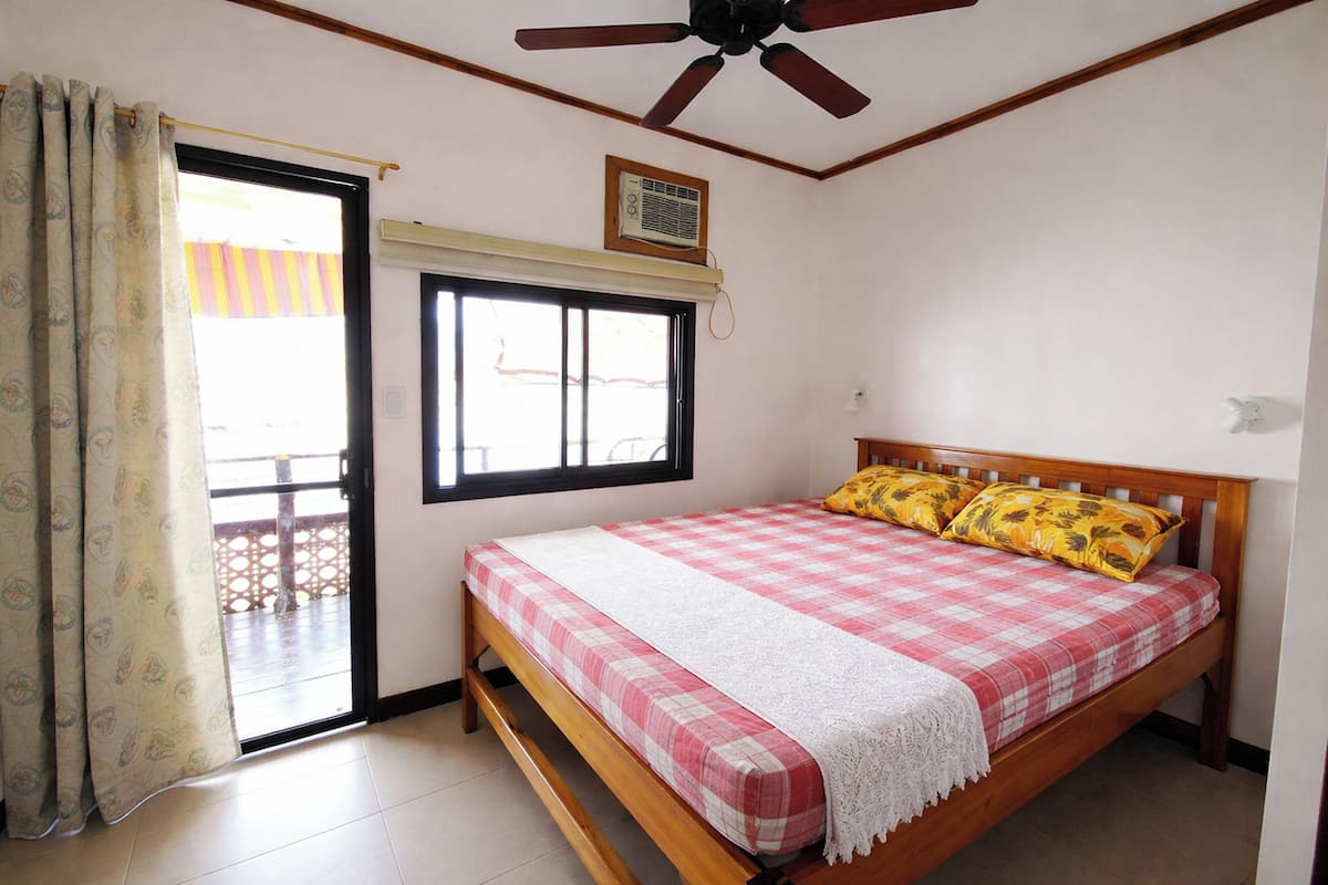 Quarto com cama, cortinas, ventilador de teto, janela e aparelho de ar condicionado.