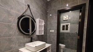 Casa de banho moderna com lavatório retangular, espelho redondo e sanita visível através de uma porta de vidro.