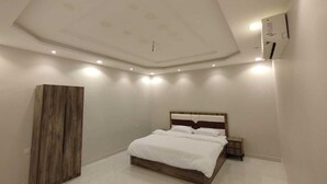 Quarto com cama, guarda-roupa, mesa de cabeceira, iluminação embutida no teto e ar condicionado.