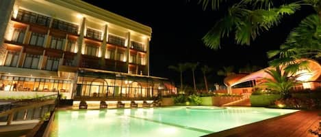 Um hotel com piscina, várias varandas e fachada bem iluminada.