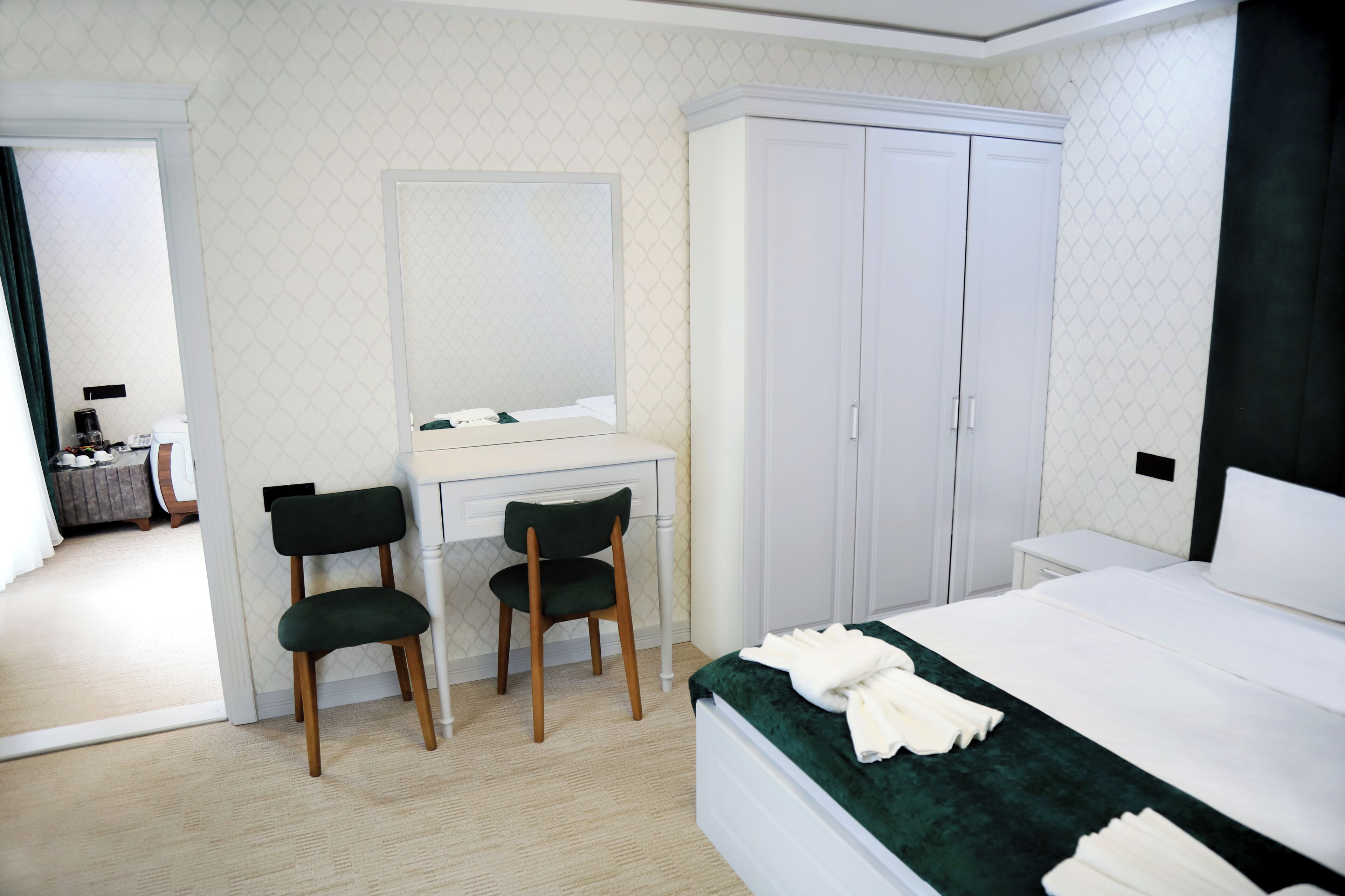 Quarto de hotel com uma cama, uma escrivaninha com duas cadeiras, um guarda-roupa e um espelho.