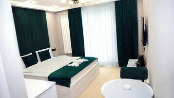 Quarto de hotel moderno com uma cama grande, uma mesa pequena, uma cadeira e uma televisão presa na parede.