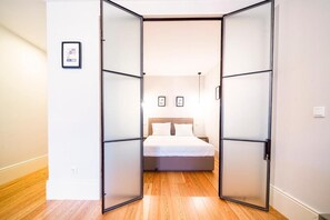 Quarto com cama, mesa de cabeceira e luminária na parede.
