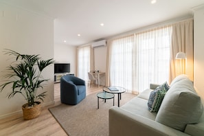 Uma sala de estar moderna com um sofá, poltrona, televisão e um vaso de planta.