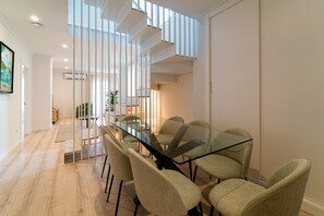 Uma área de jantar moderna com mesa e cadeiras de vidro, uma escada e vista para o exterior.