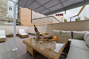 Uma área externa com mesa de vidro, móveis de vime e um sofá acolchoado.