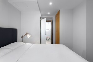 Quarto de hotel moderno com uma cama grande, uma luminária de mesa e um guarda-roupa de madeira.