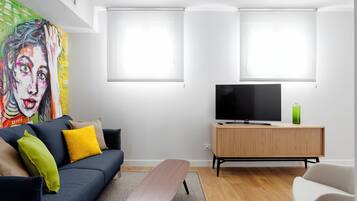 Uma sala de estar moderna com um sofá, uma mesa de centro, uma TV em um armário de madeira e um quadro colorido na parede.