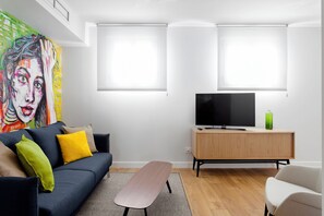 Uma sala de estar moderna com um sofá, uma mesa de centro, uma TV em um armário de madeira e um quadro colorido na parede.