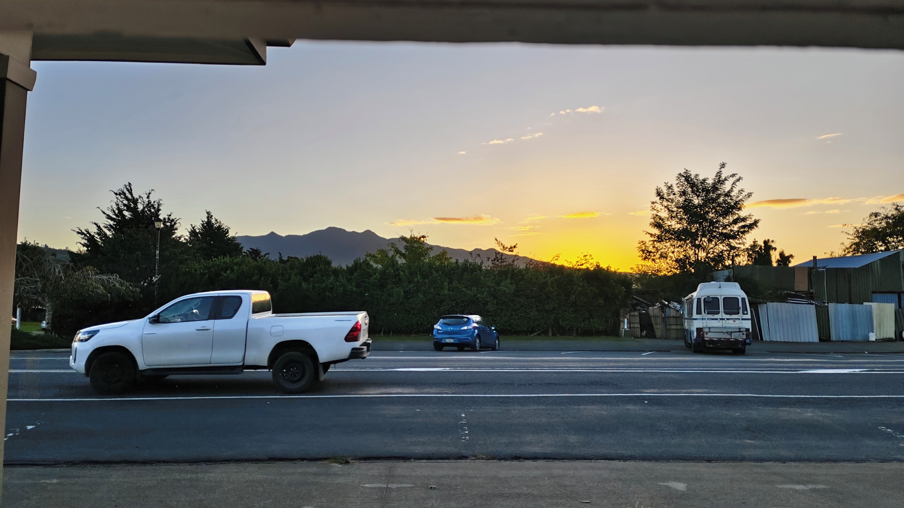 Um estacionamento com uma caminhonete branca, um carro azul e uma van branca.