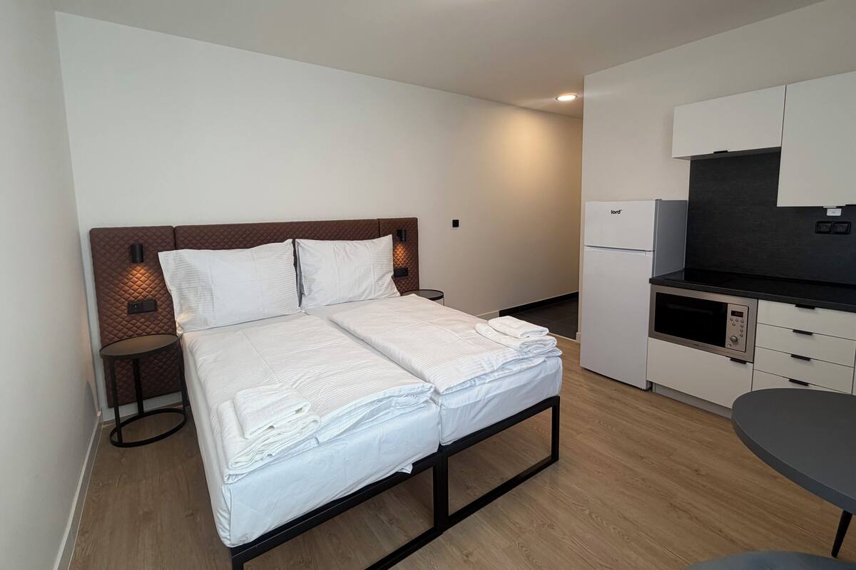 Quarto compacto com cama, pequena cozinha e área de refeições.