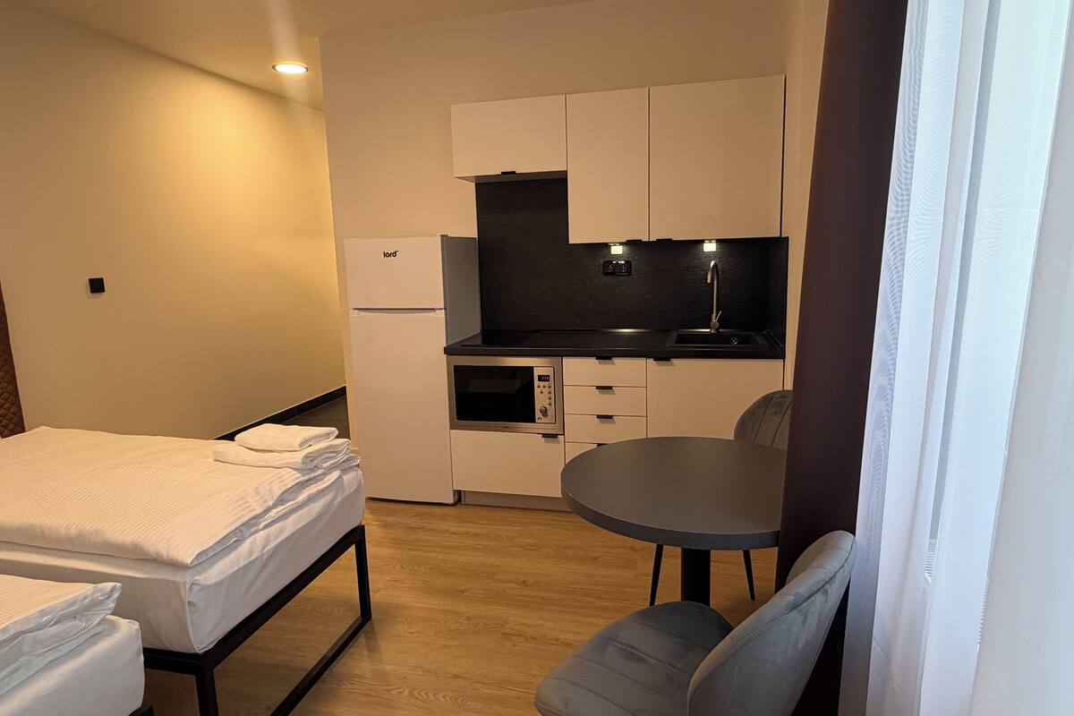 Quarto compacto com cama, pequena cozinha, mesa de jantar e uma cadeira.